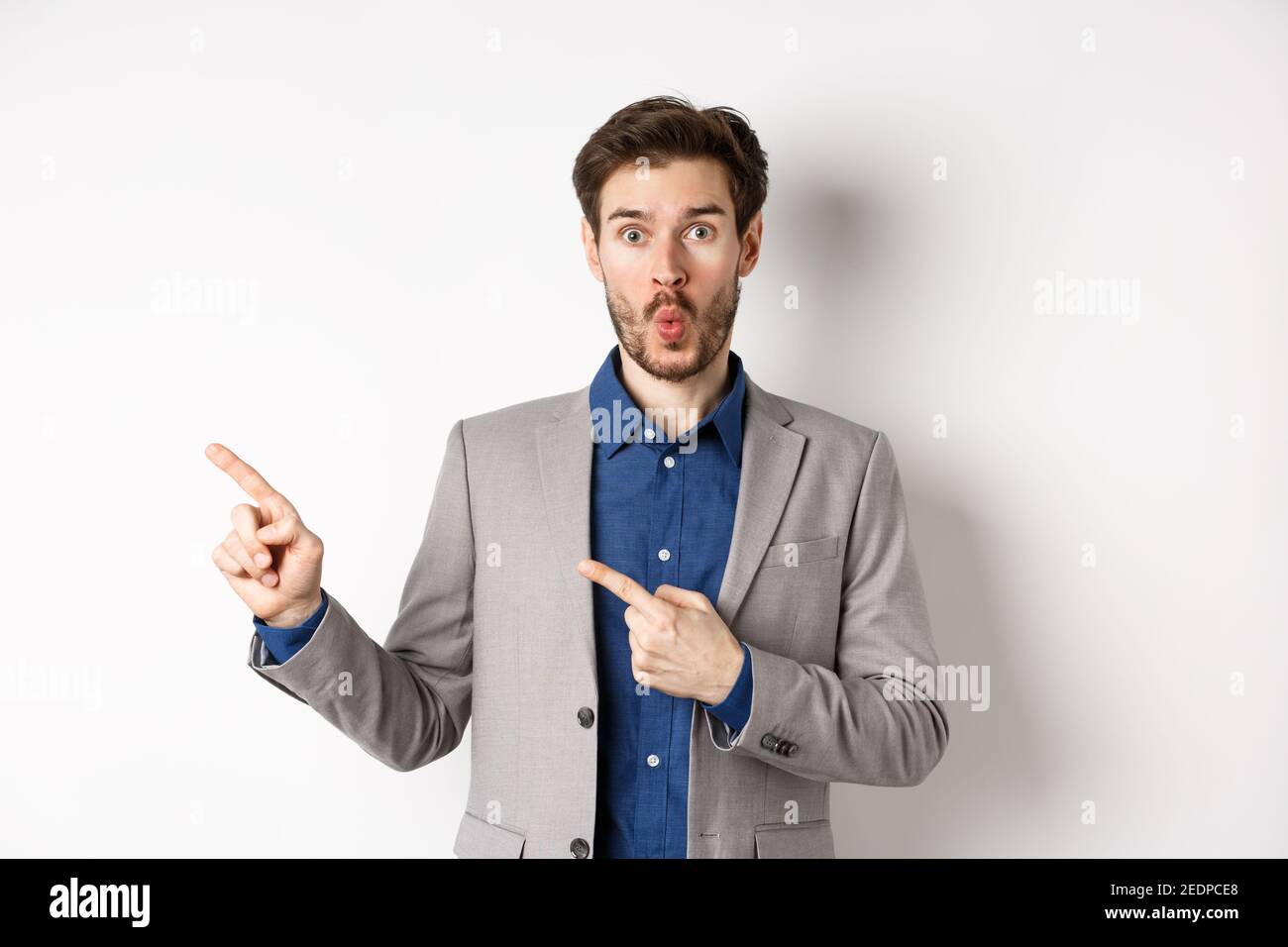 Excited handsome man in suit pointing fingers left at banner and saying ...