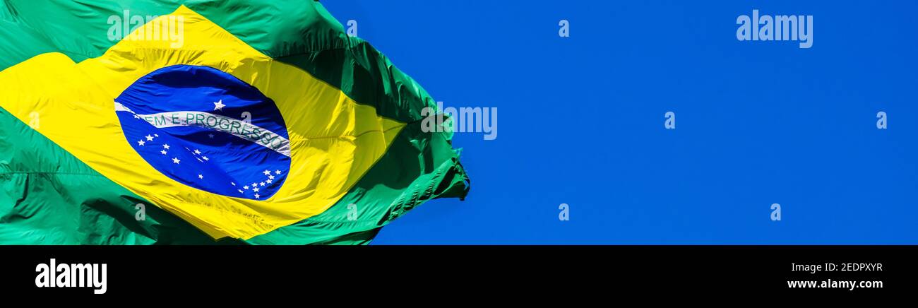Closeup shot of a Brazil flag waving in the wind against a blue sky ...