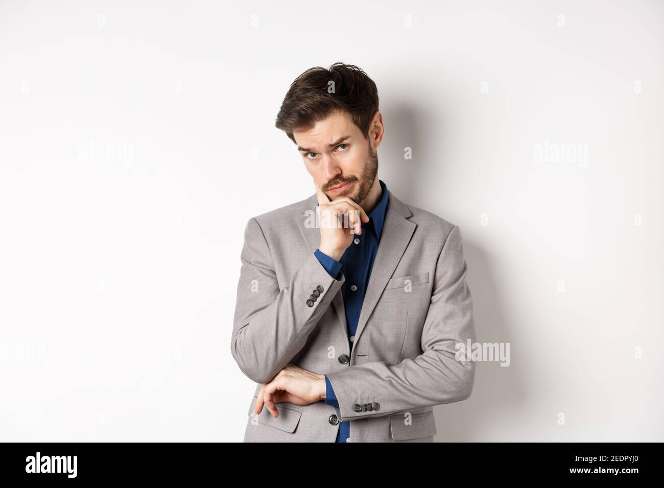 Hesitant businessman in suit making decision, looking pensive at camera ...