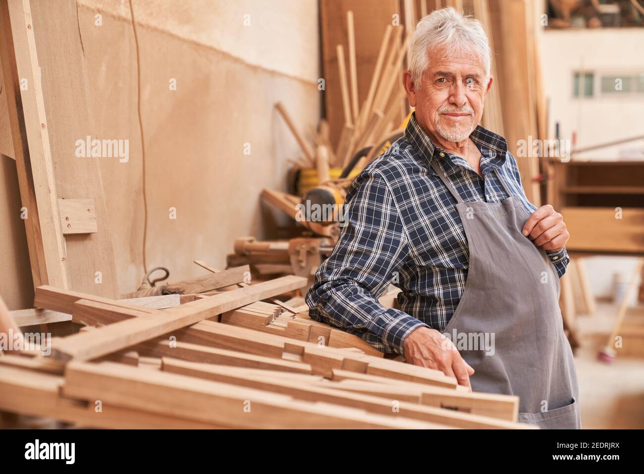 Satisfied senior carpenter as a craftsman portrait in his workshop with ...