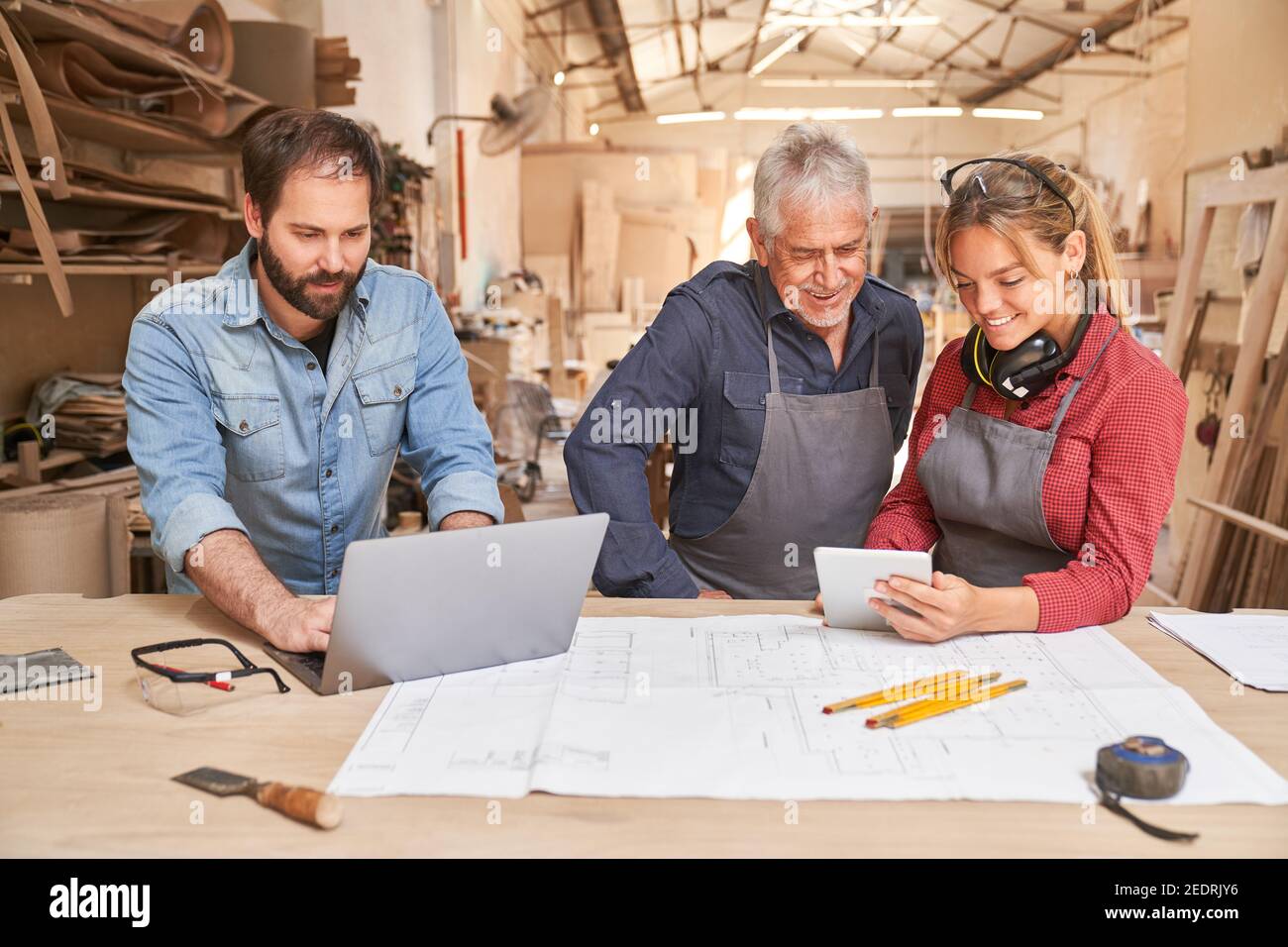 Group of craftsmen as carpenter team using laptop computer in workshop ...