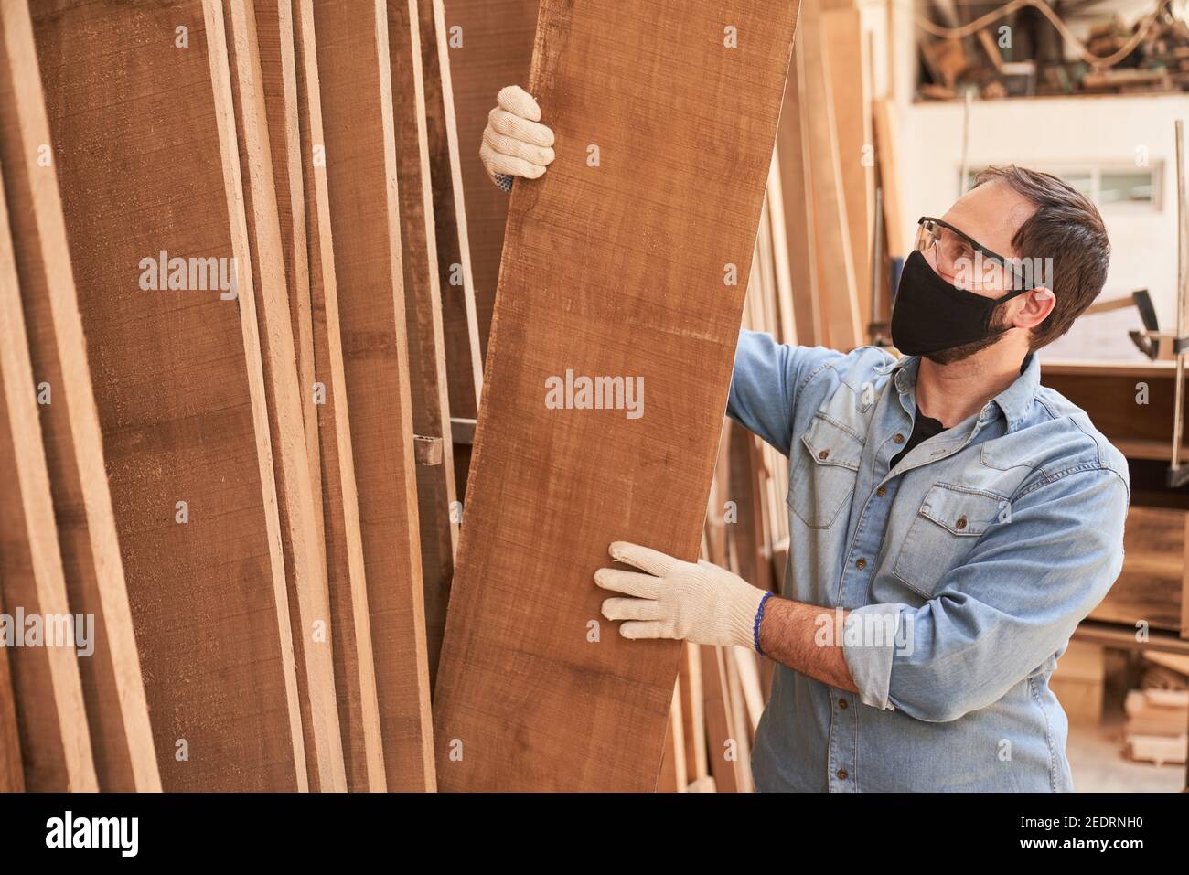 Craftsman as a carpenter with face mask in the wood warehouse selects a ...
