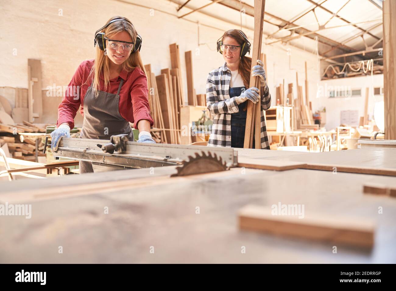 Woman as a craftsman trainee works on the circular saw of the joinery ...