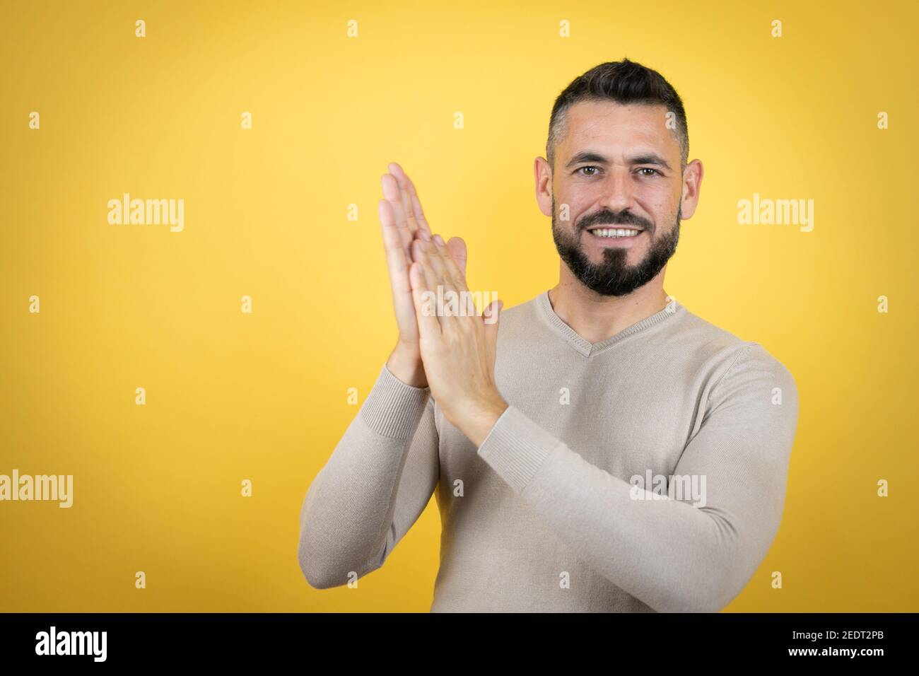 Handsome man with beard wearing sweater over yellow background clapping ...