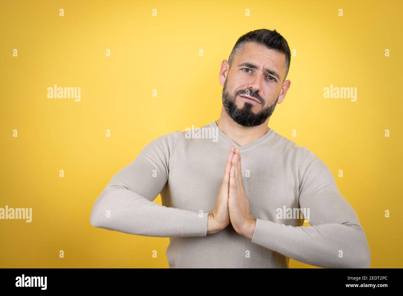 Handsome man with beard wearing sweater over yellow background begging ...