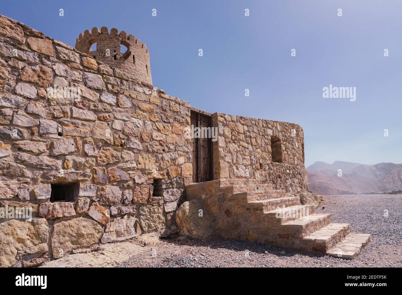 Stone wall of a small medieval arabian fort with wooden door and stone ...