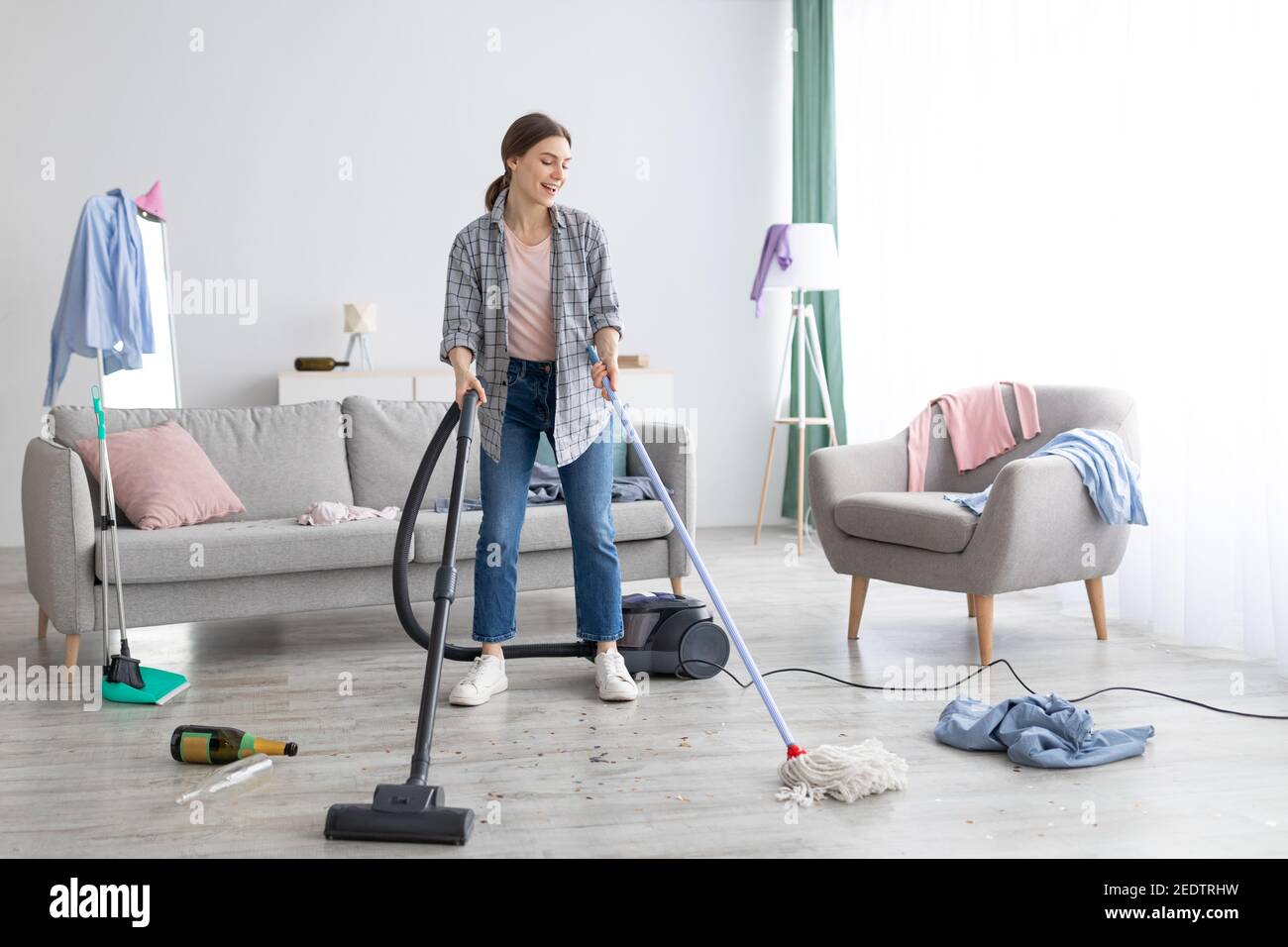 Happy young woman vacuuming her house after party, copy space. Domestic ...