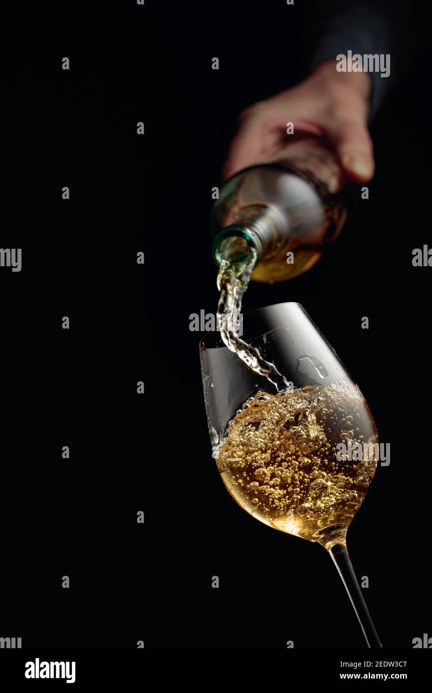 Pouring white wine in a glass goblet. Black background with copy space ...