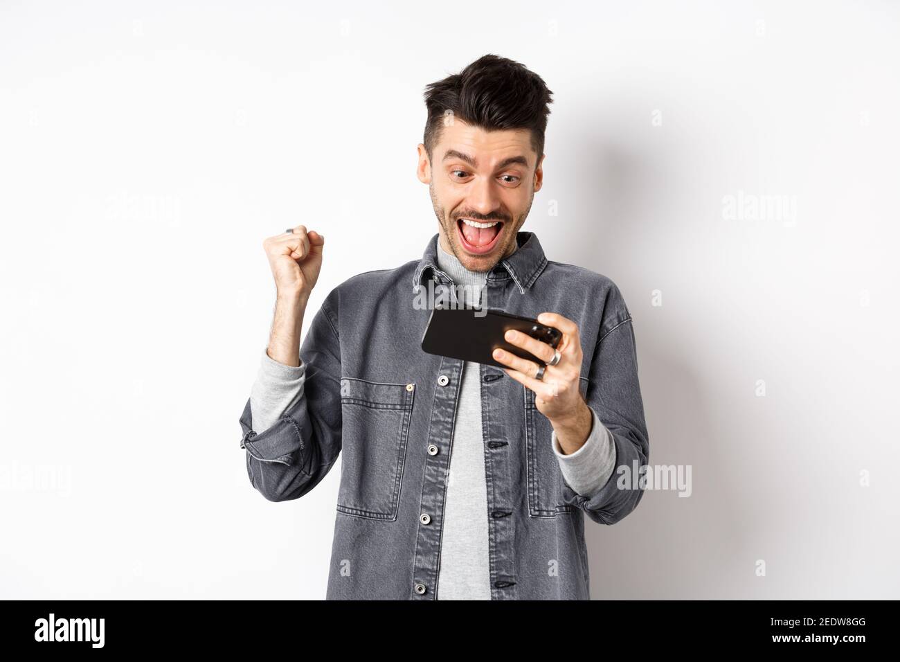 Happy man shouting yes, winning video game on mobile phone and ...