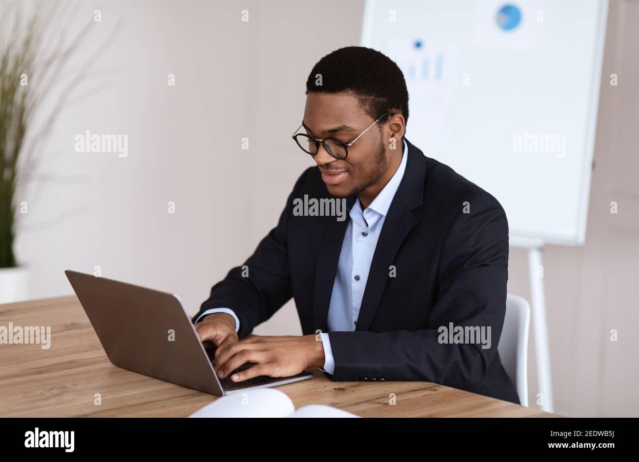 Young black manager smiling while working with laptop, office interior ...