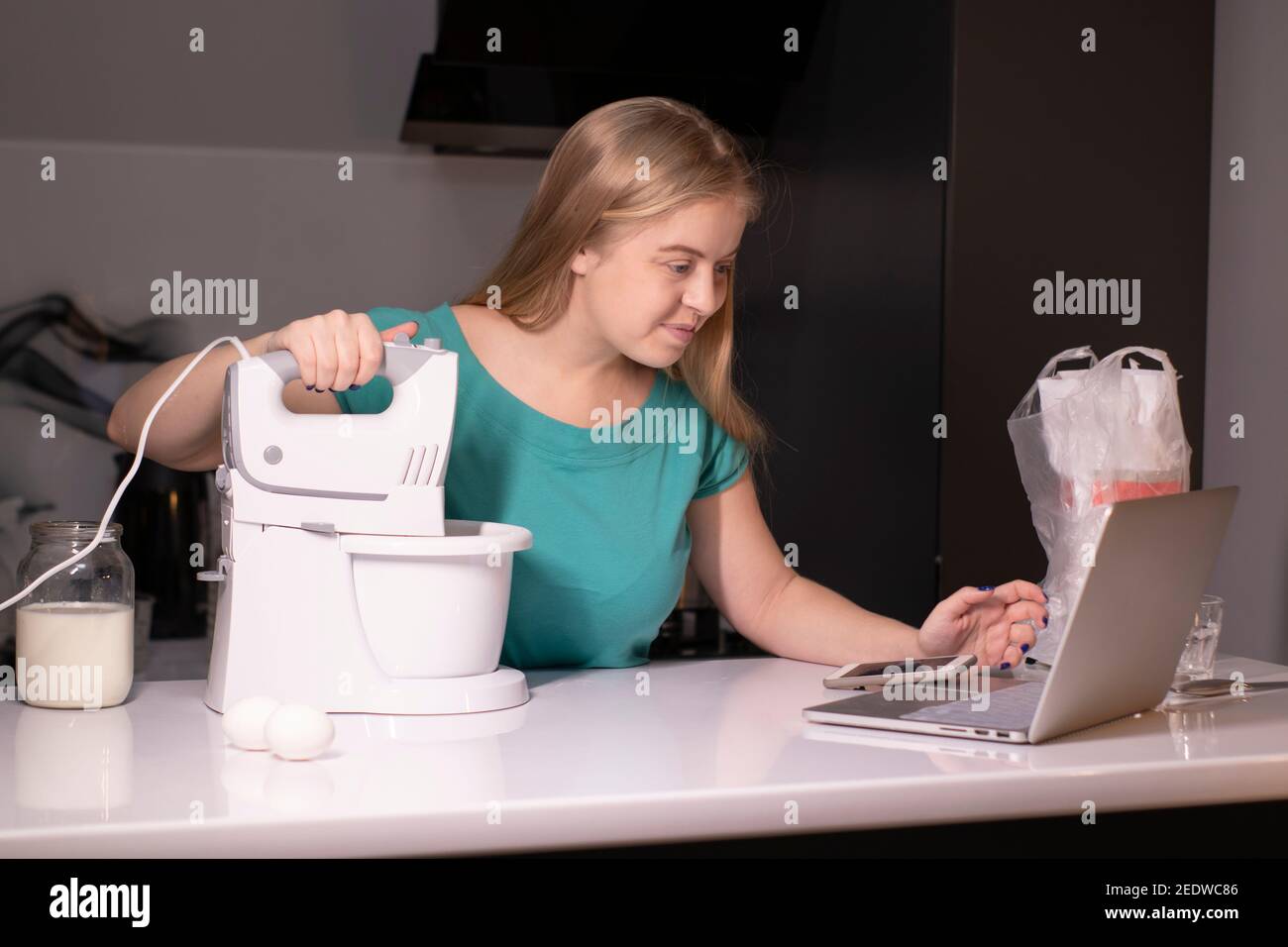 Young blonde woman watching recipe on laptop while cooking lunch in ...
