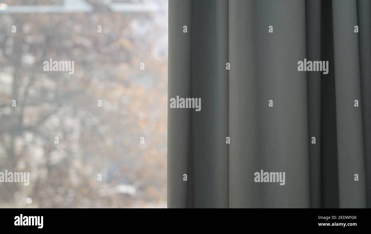 Selective focus of a gray curtain of a window with trees visible ...