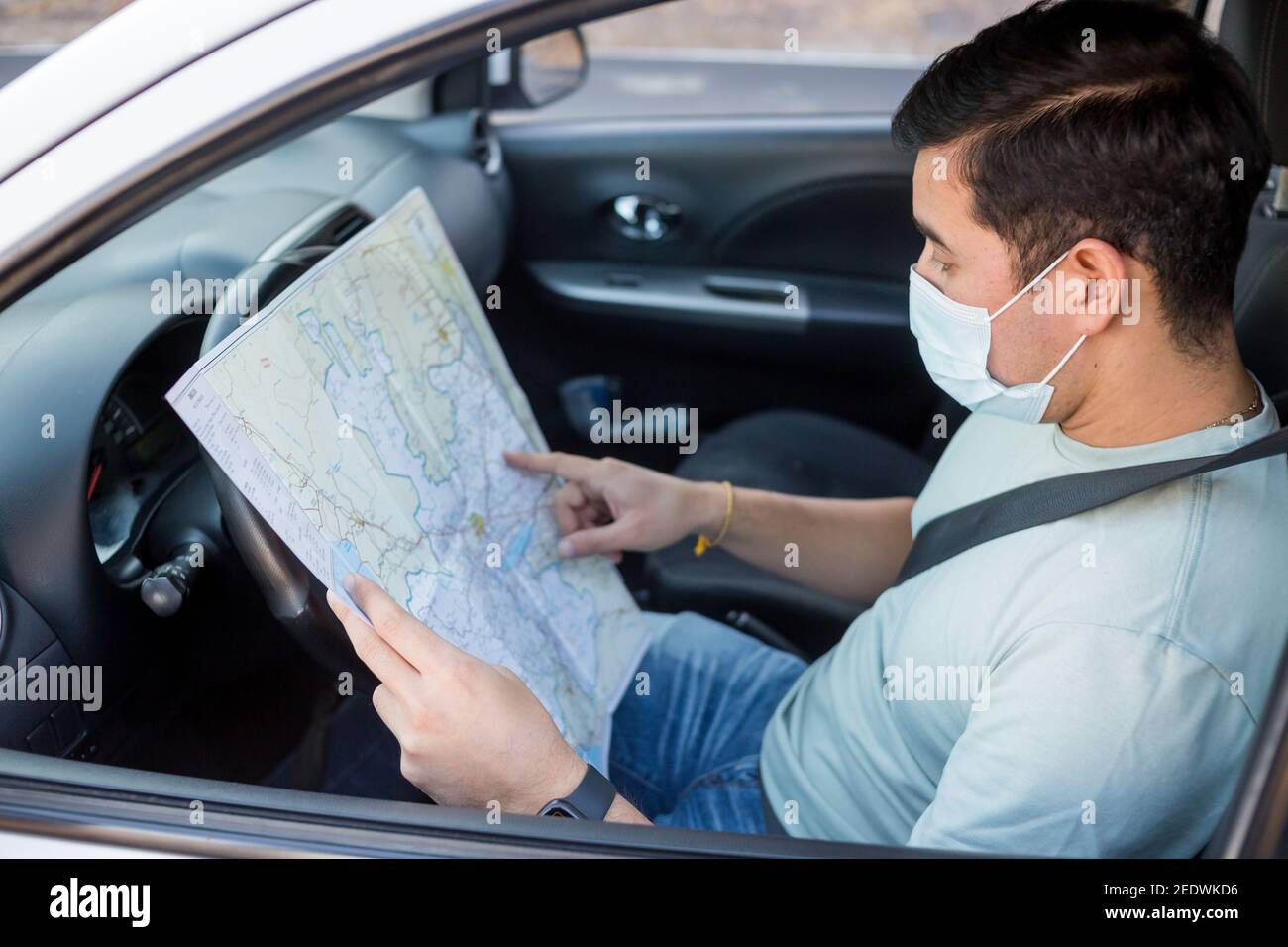 Male traveler wearing a sanitary mask sitting in his car looking at ...