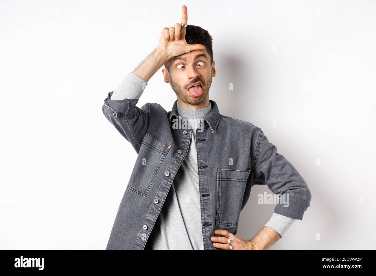 Funny young man making faces and showing tongue with loser sign on ...