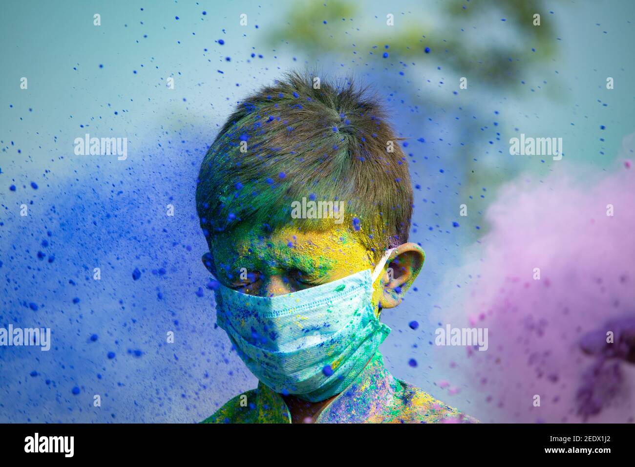 Portrait shot of young kid with face mask standing while colorful Holi ...
