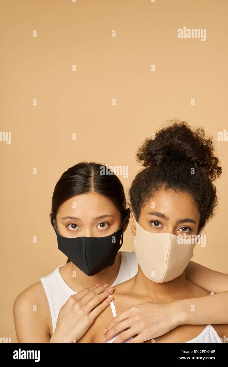 Portrait of two adorable young diverse women wearing protective facial ...