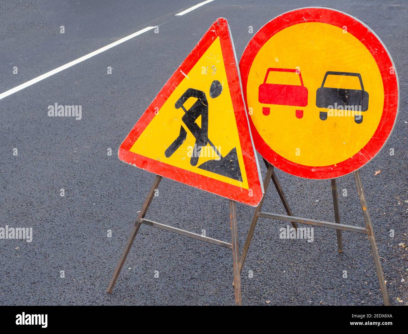 Triangular and circular road signs stand on freshly asphalted road with ...