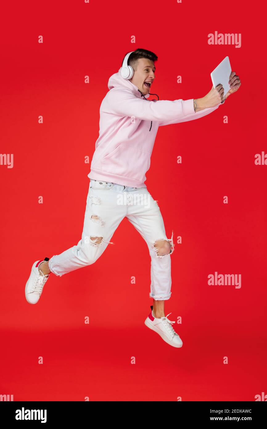 Jumping high with headphones. Caucasian man's portrait isolated on red ...