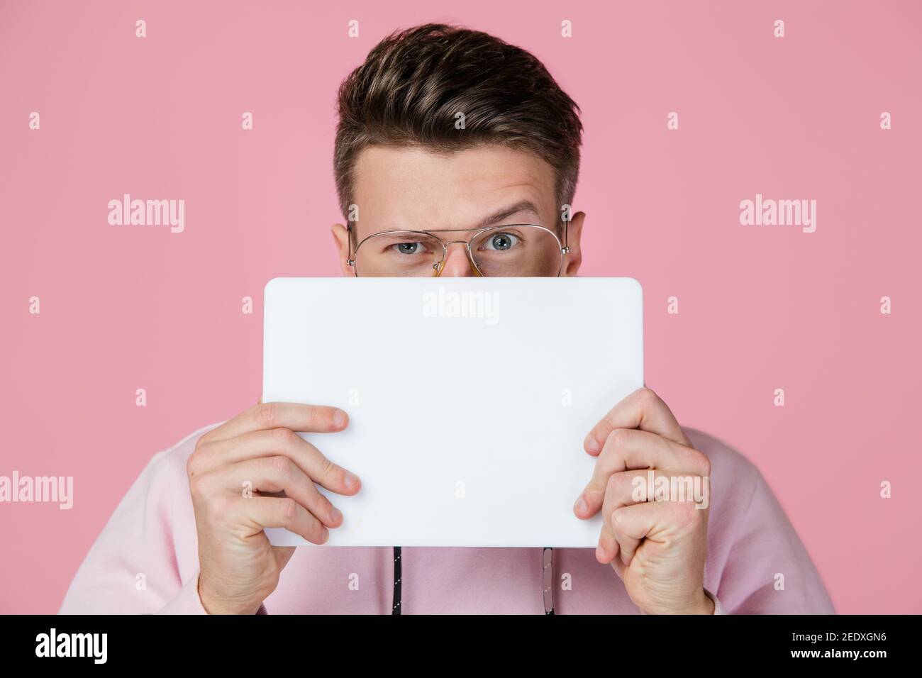 Hising behind the tablet. Caucasian man's portrait isolated on pink ...