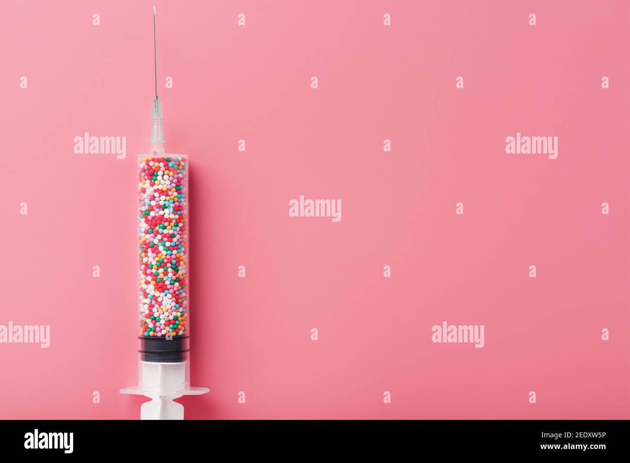 Medical Syringe filled with colorful balloons on a pink background with ...