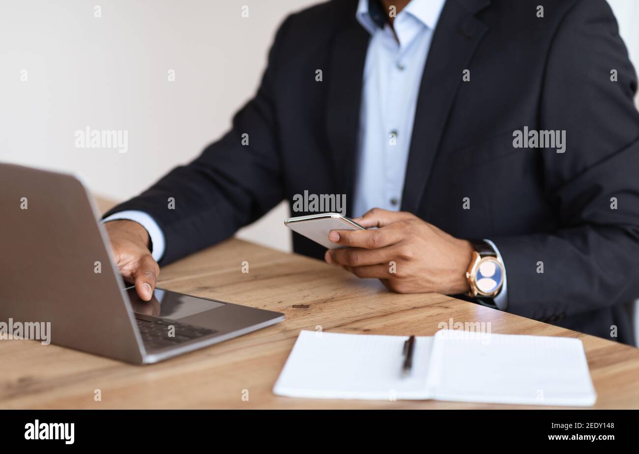 Unrecognizable black manager holding smartphone, using laptop Stock ...