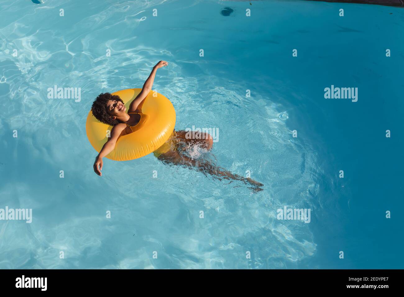 Mixed race woman sunbathing on inflatable in swimming pool. Hanging out ...
