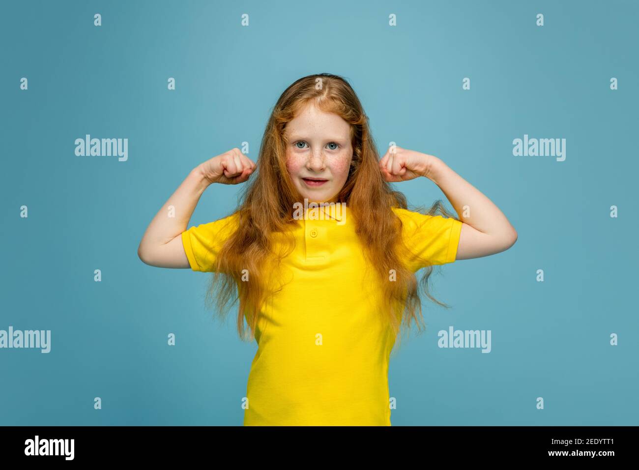 Strong, powerful. Happy, smiley redhair girl isolated on blue studio ...