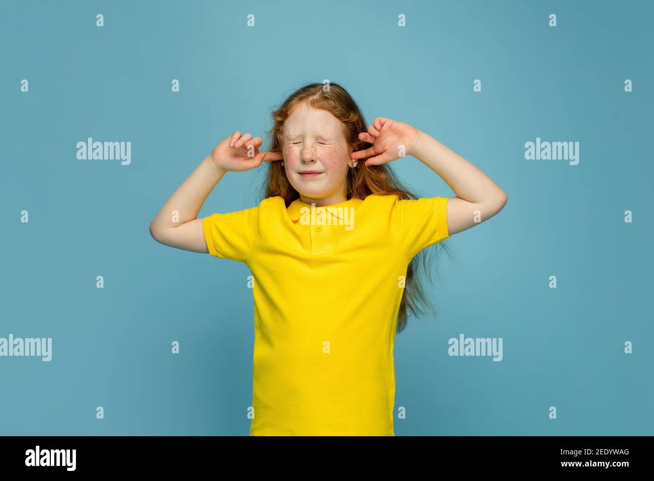 Closing ears. Happy, smiley redhair girl isolated on blue studio ...
