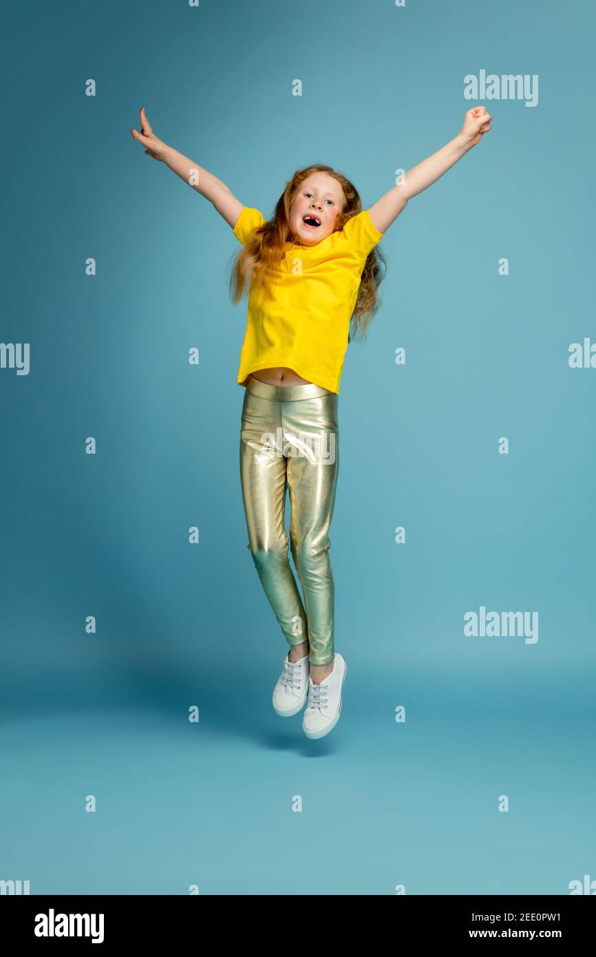 Jumping high. Happy, smiley redhair girl isolated on blue studio ...