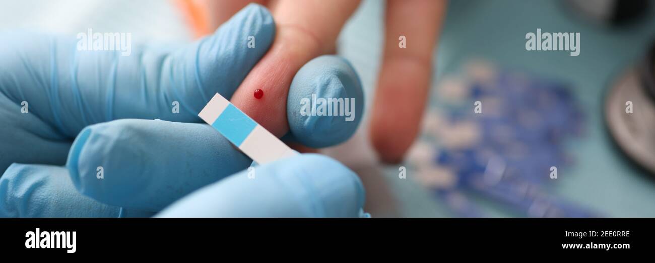 Doctor holding test strip near patients finger with drop of blood in ...