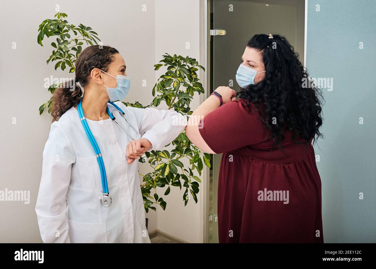 Overweight woman and her doctor wearing medical masks greeting each ...