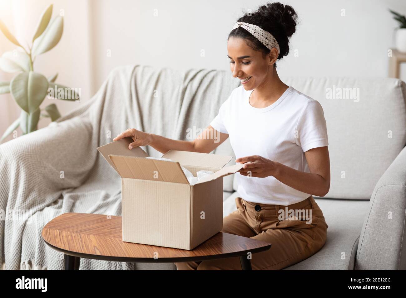 Happy young woman unpacking delivery box, home interior Stock Photo - Alamy