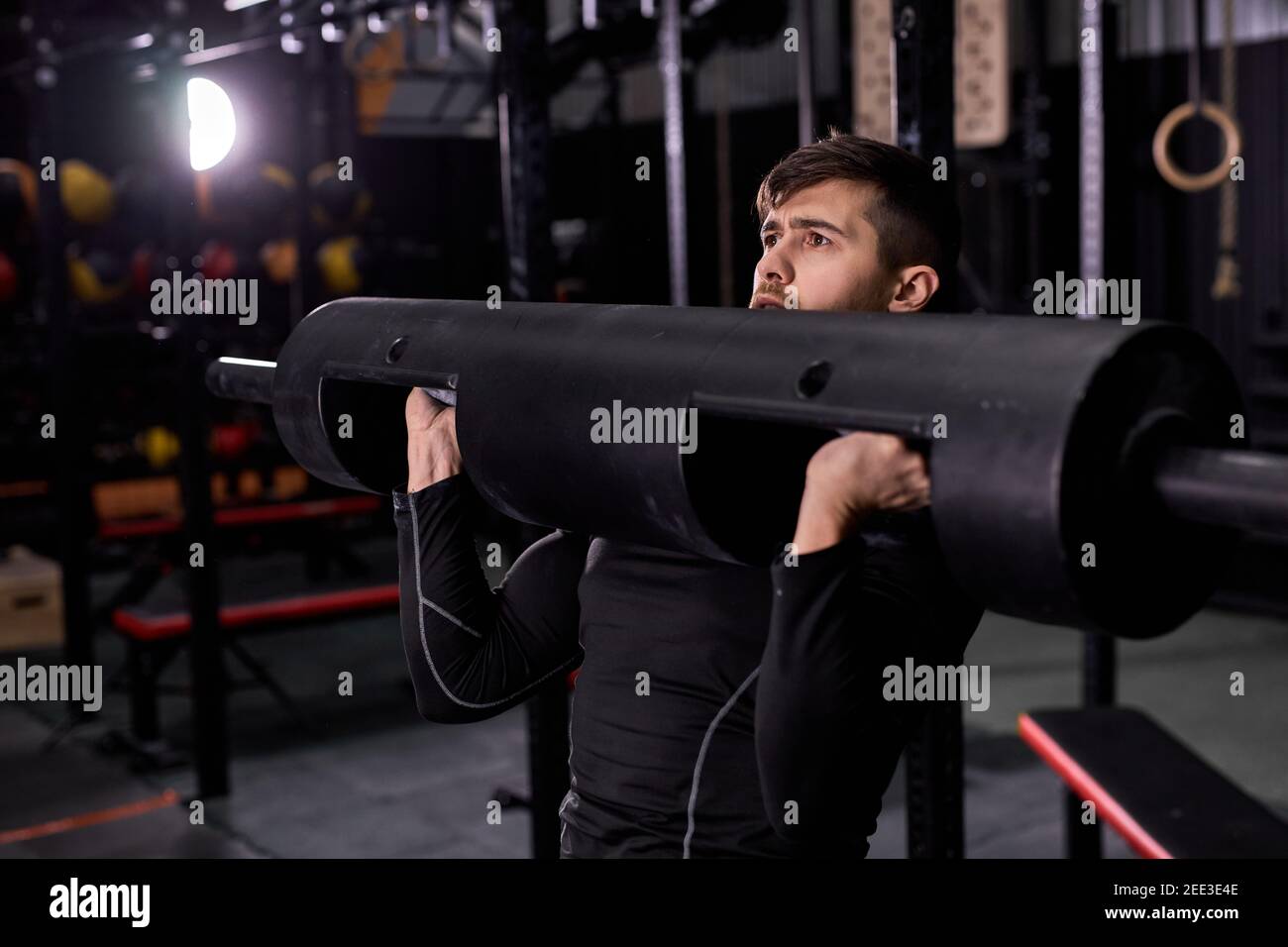 powerful athlete raising weights up, using sportive equipment in moder ...