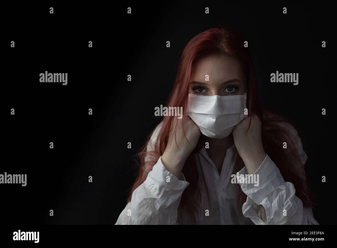 Low key portrait of angry redhead young woman with a medical face mask ...