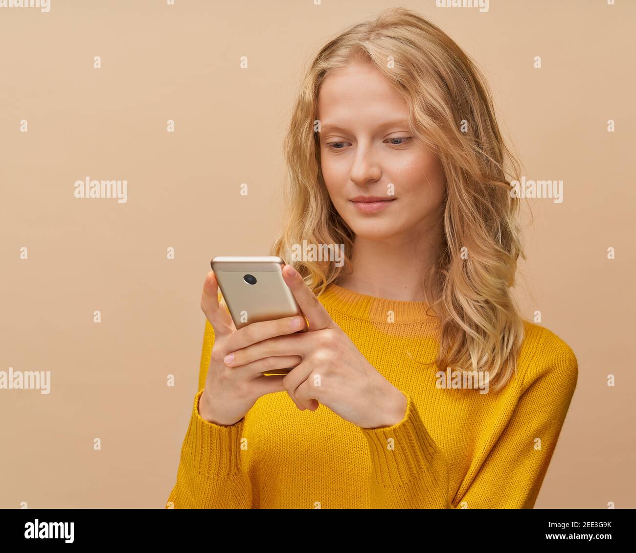 Pretty female looking social media on mobile phone standing near beige ...