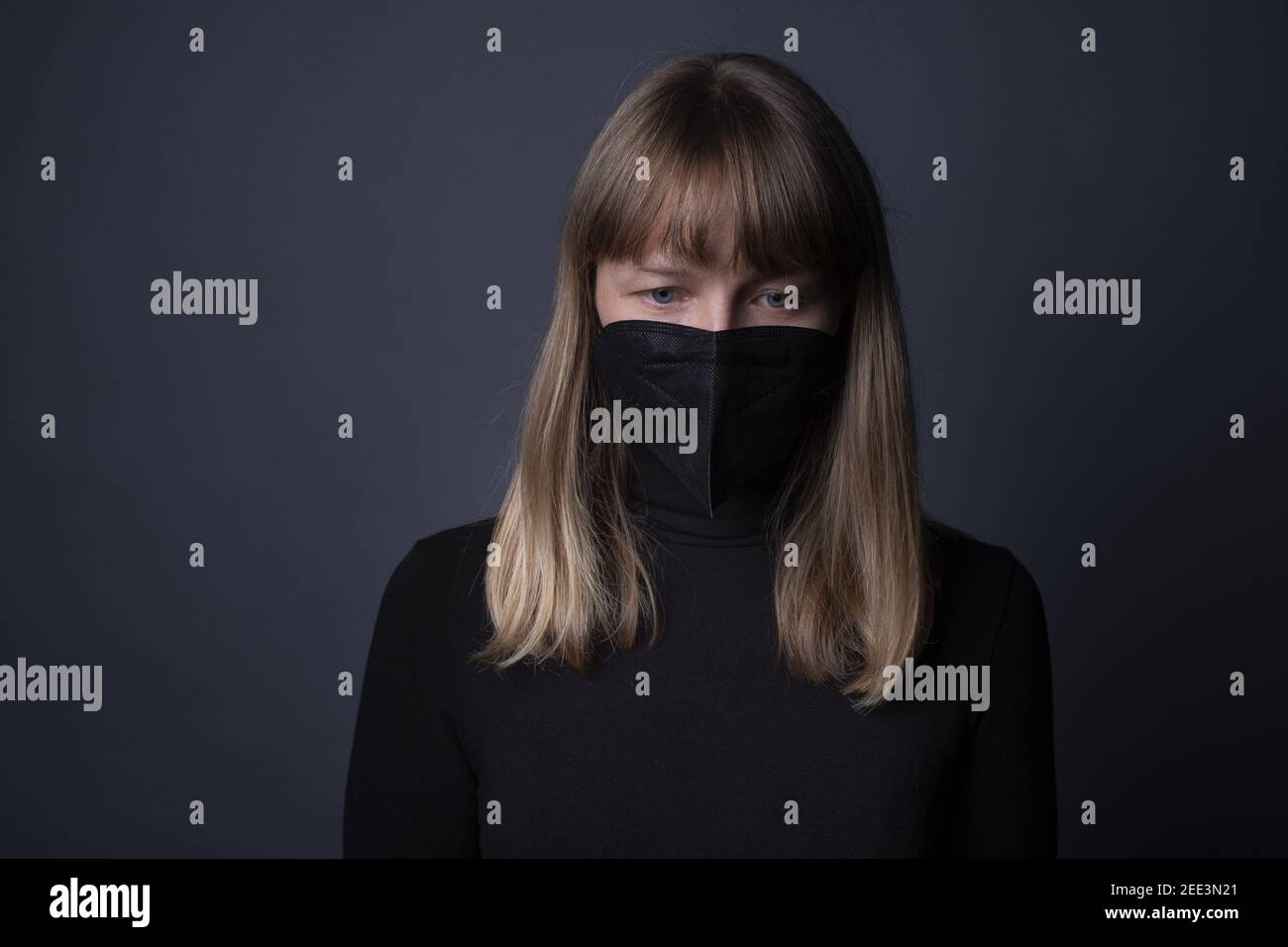 Blonde female in a black protective face mask with a sad tired ...