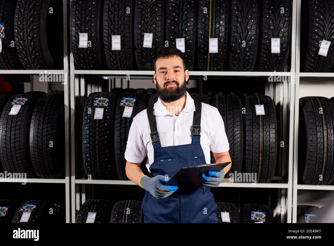 male mechanic near rack with car tires in auto store, looking at camera ...