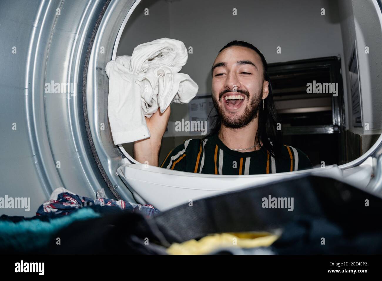 stylish young man with long hair is washing clothes in a laundromat ...