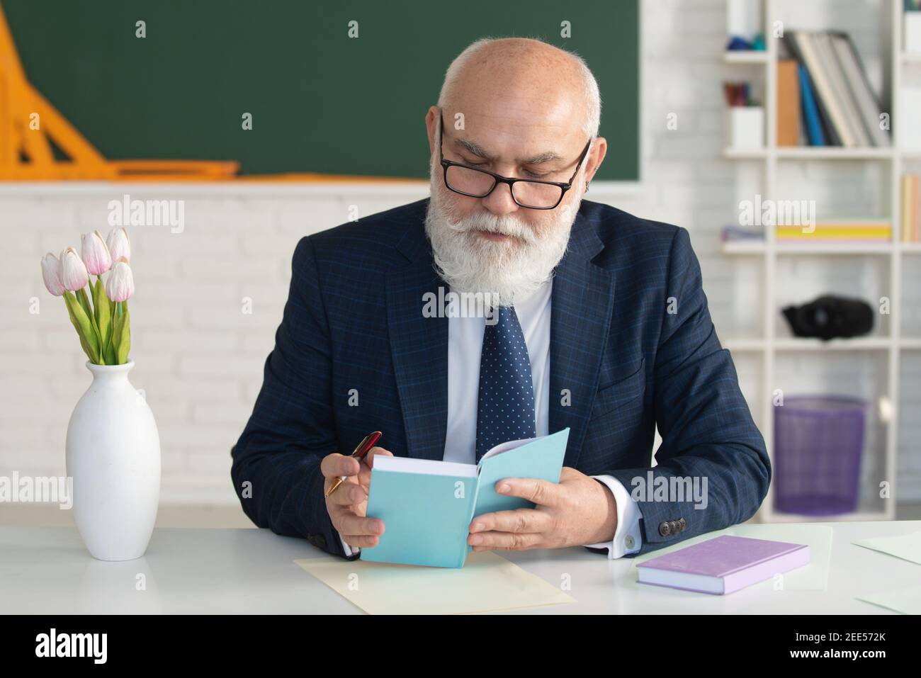 Older male teacher standing in front of a chalkboard in a classroom ...