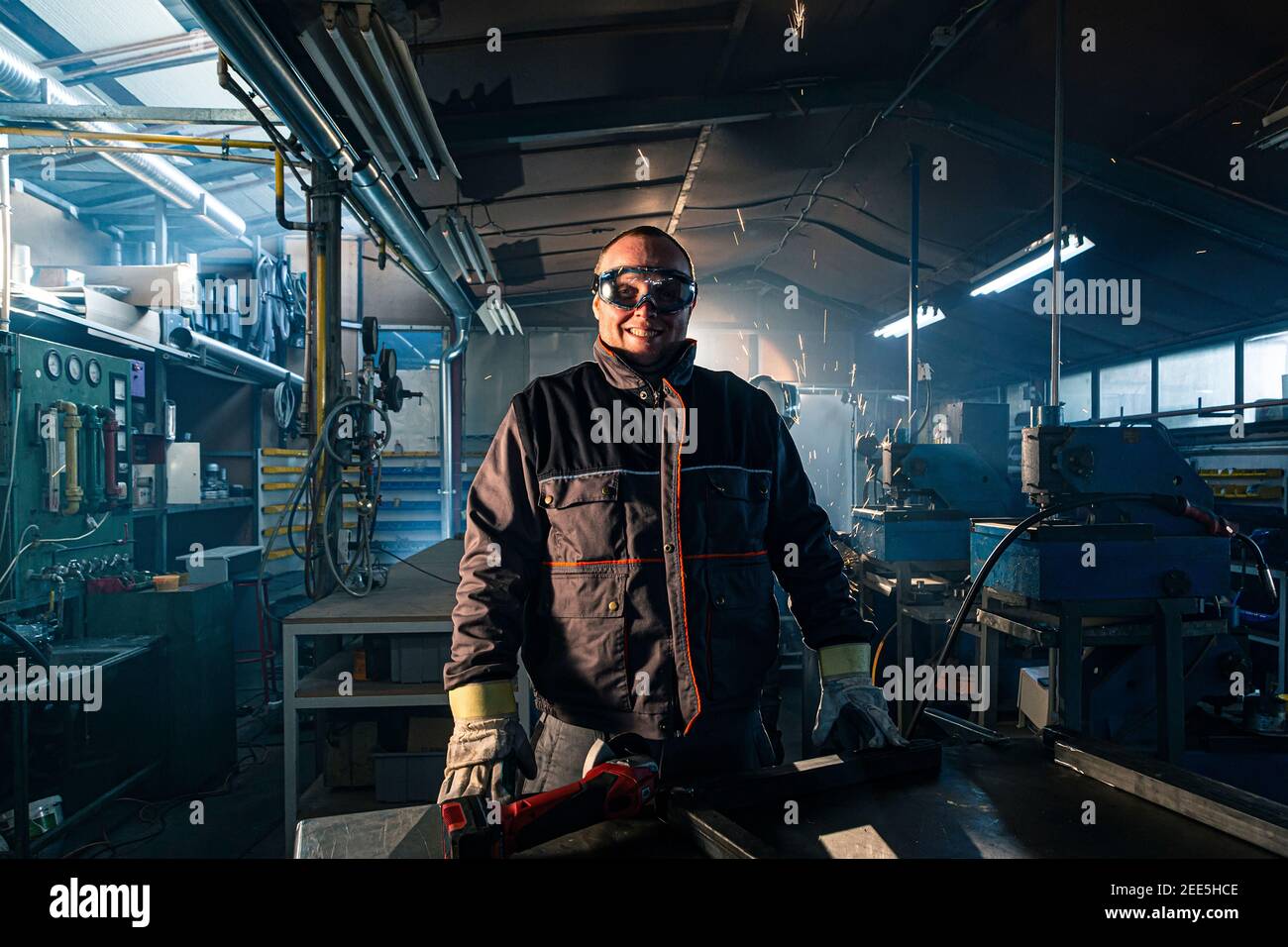 The handyman for grinding poses with a smile in the workshop with ...