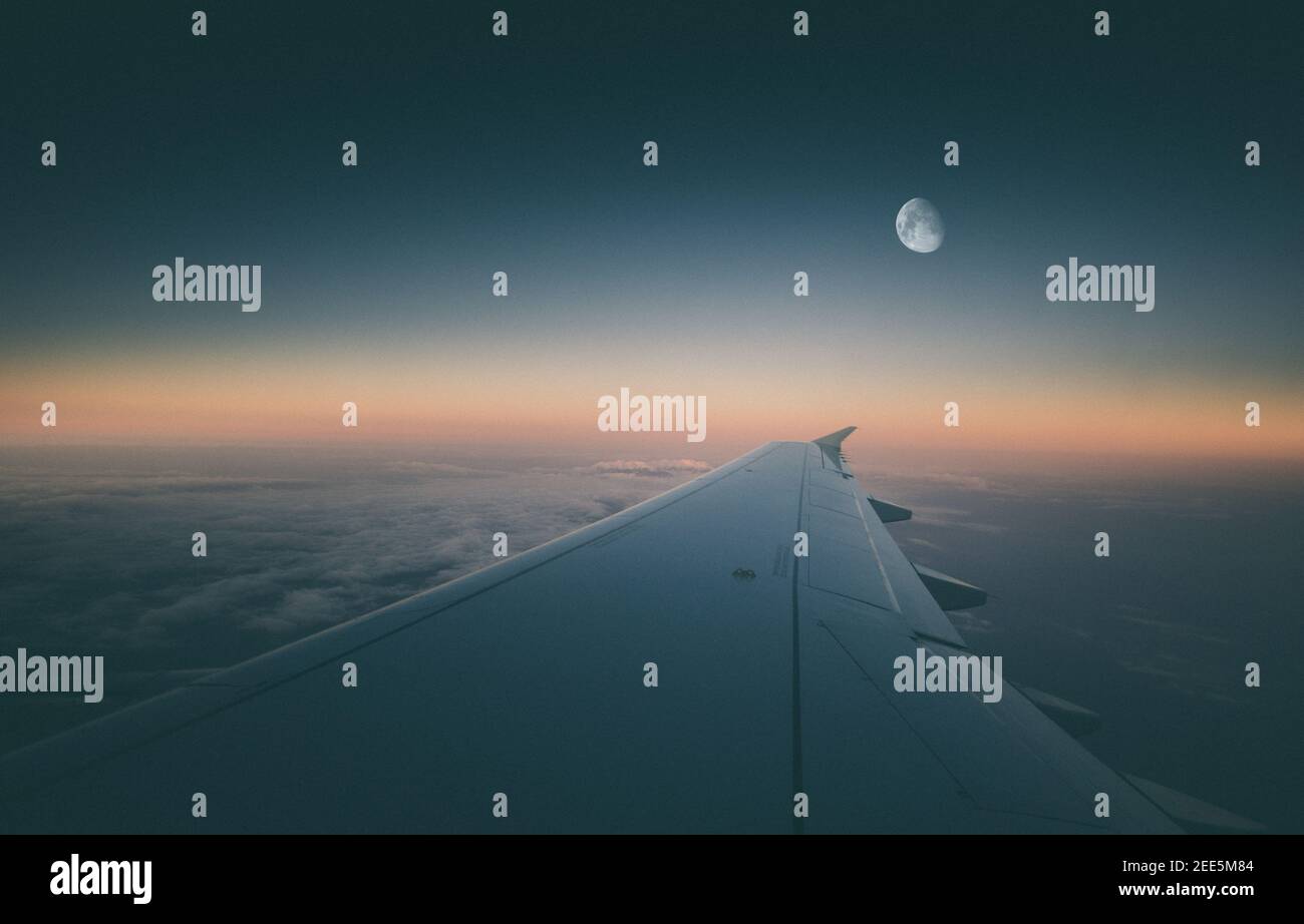 Wing of an airplane flying in the early morning with the moon yet in ...