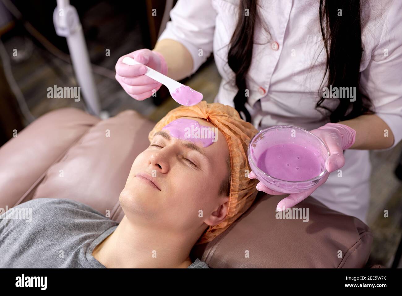 facial mask of man in spa salon, handsome male get beauty procedure. massage on face. beautician ...