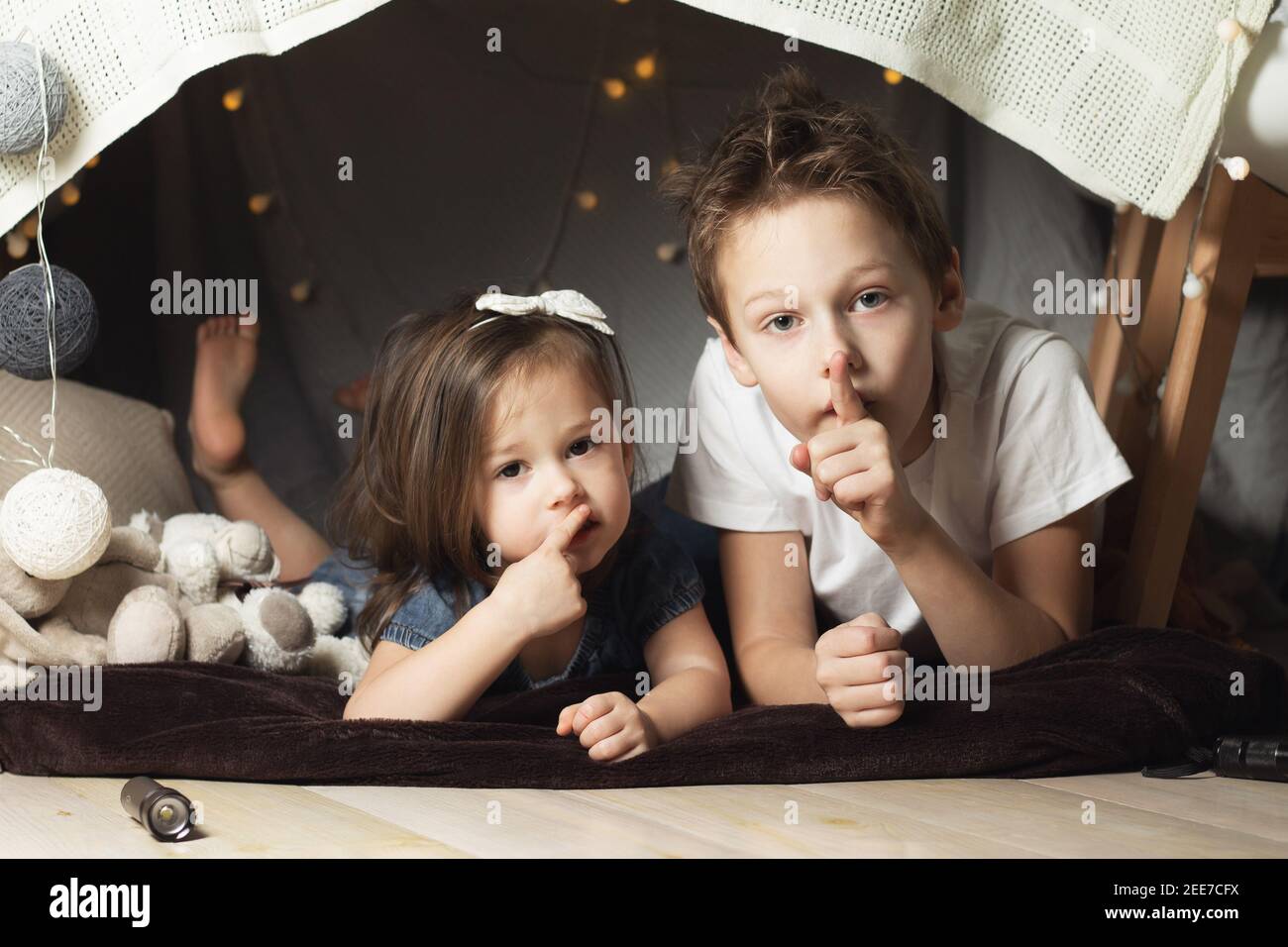 Siblings lie in hut of chairs and blankets. Brother and sister show ...