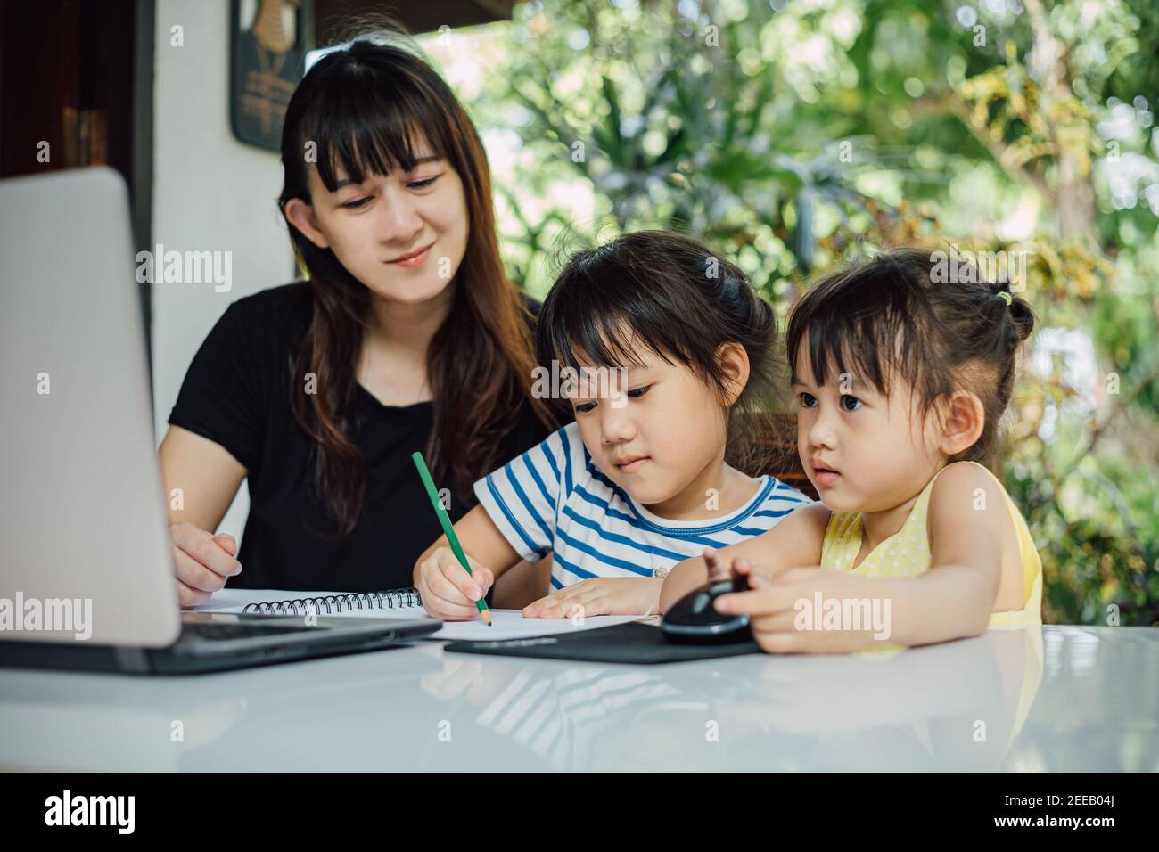 Happy family of mom and preschool daughter using laptop for remote study at home. Mother teach ...