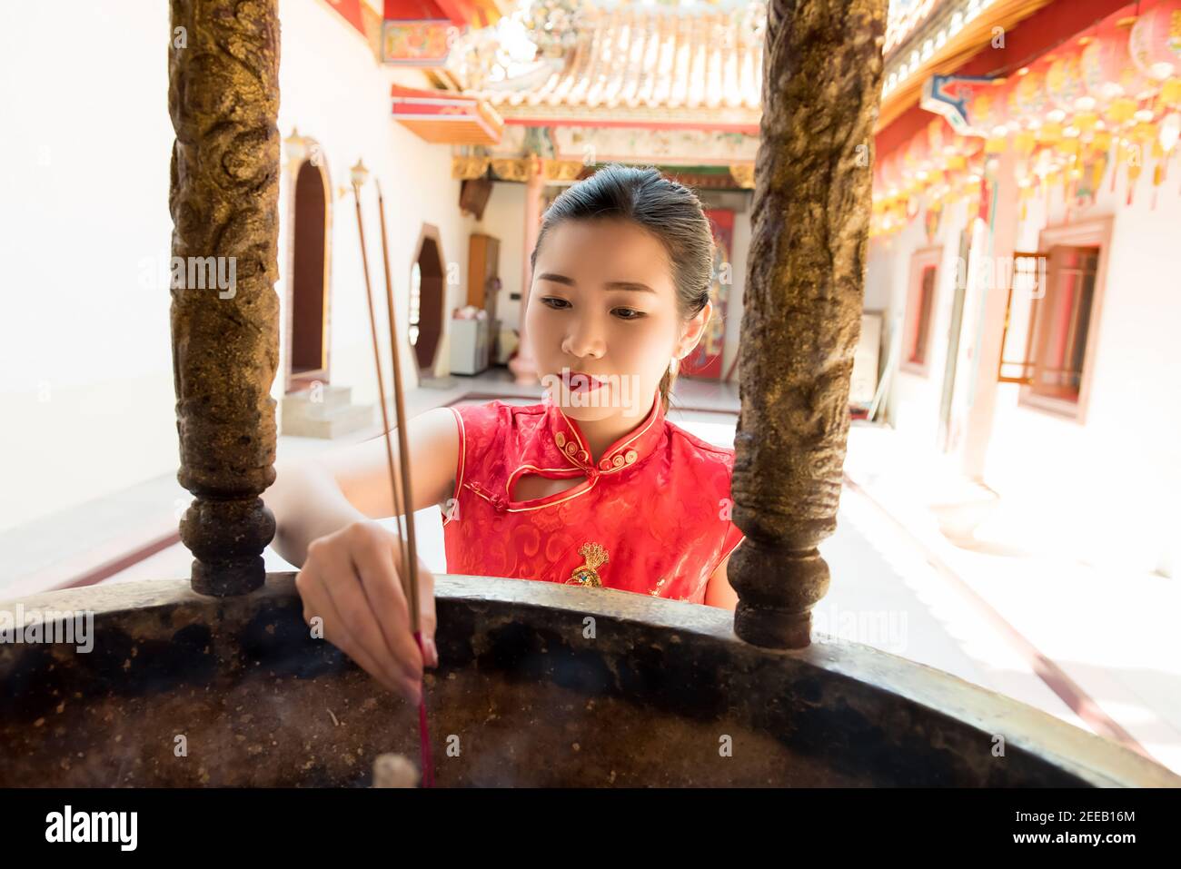 Asian woman in red qipao dress praying with incense sticks during ...
