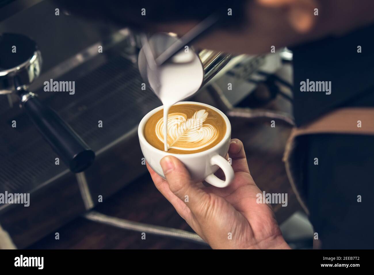Professional barista pouring steamed milk into coffee cup making ...