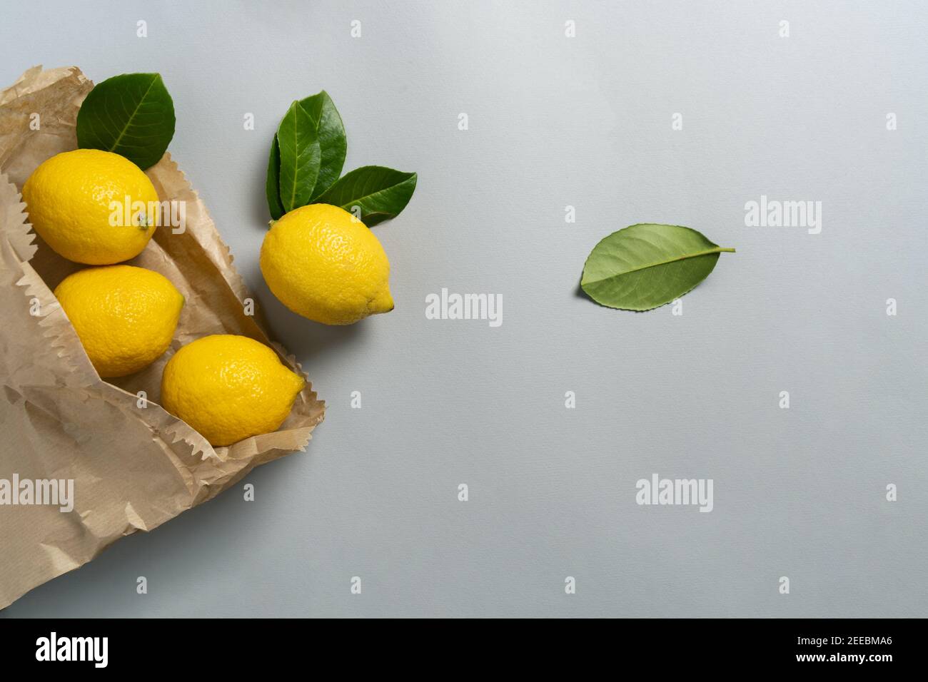 Lemons in craft paper with leaves on texture grey background with copy ...