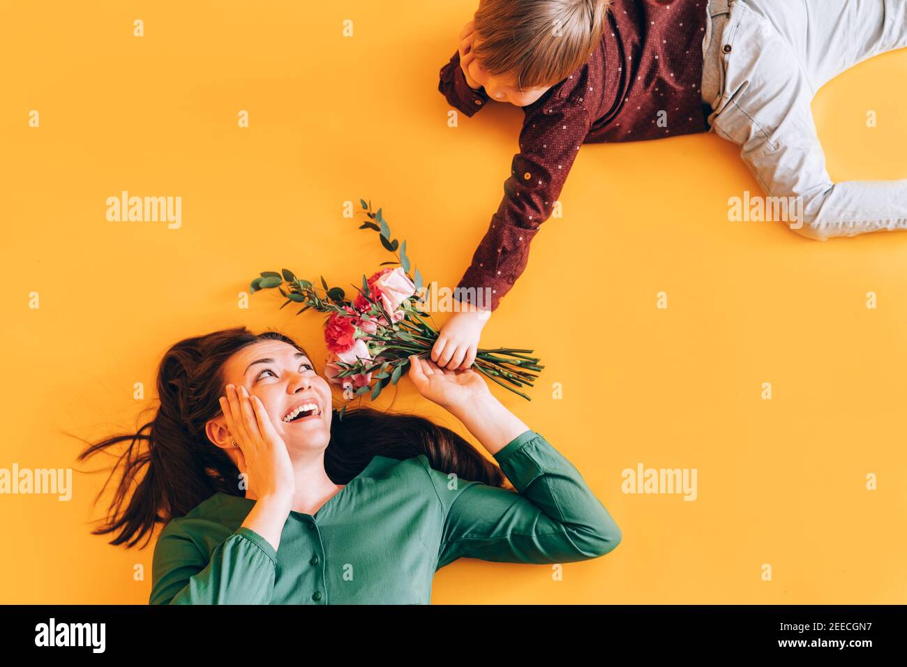 Little boy gives mom a bouquet of flowers against a yellow background ...