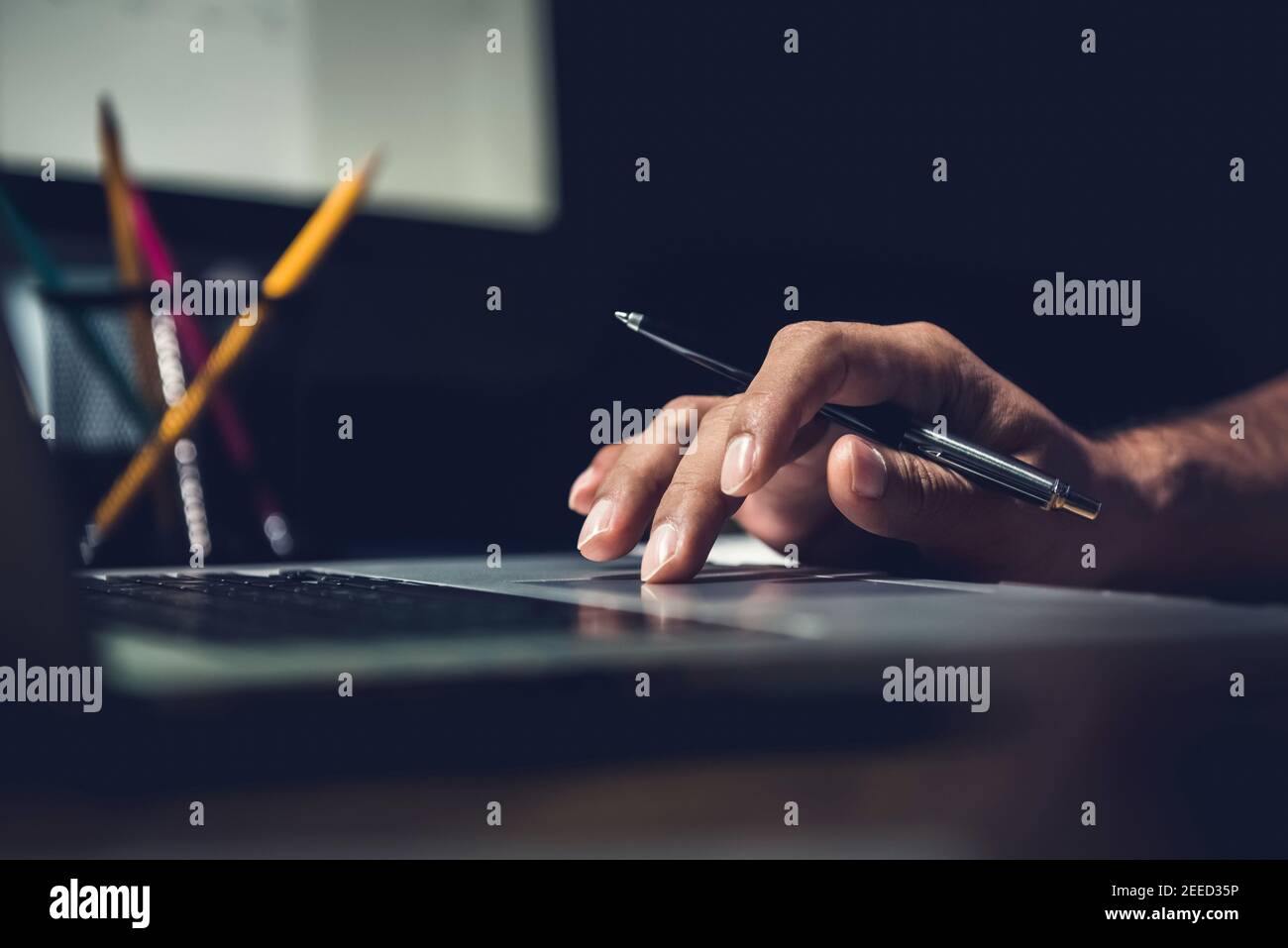 Hand of a man using laptop computer working overtime at his desk in the ...