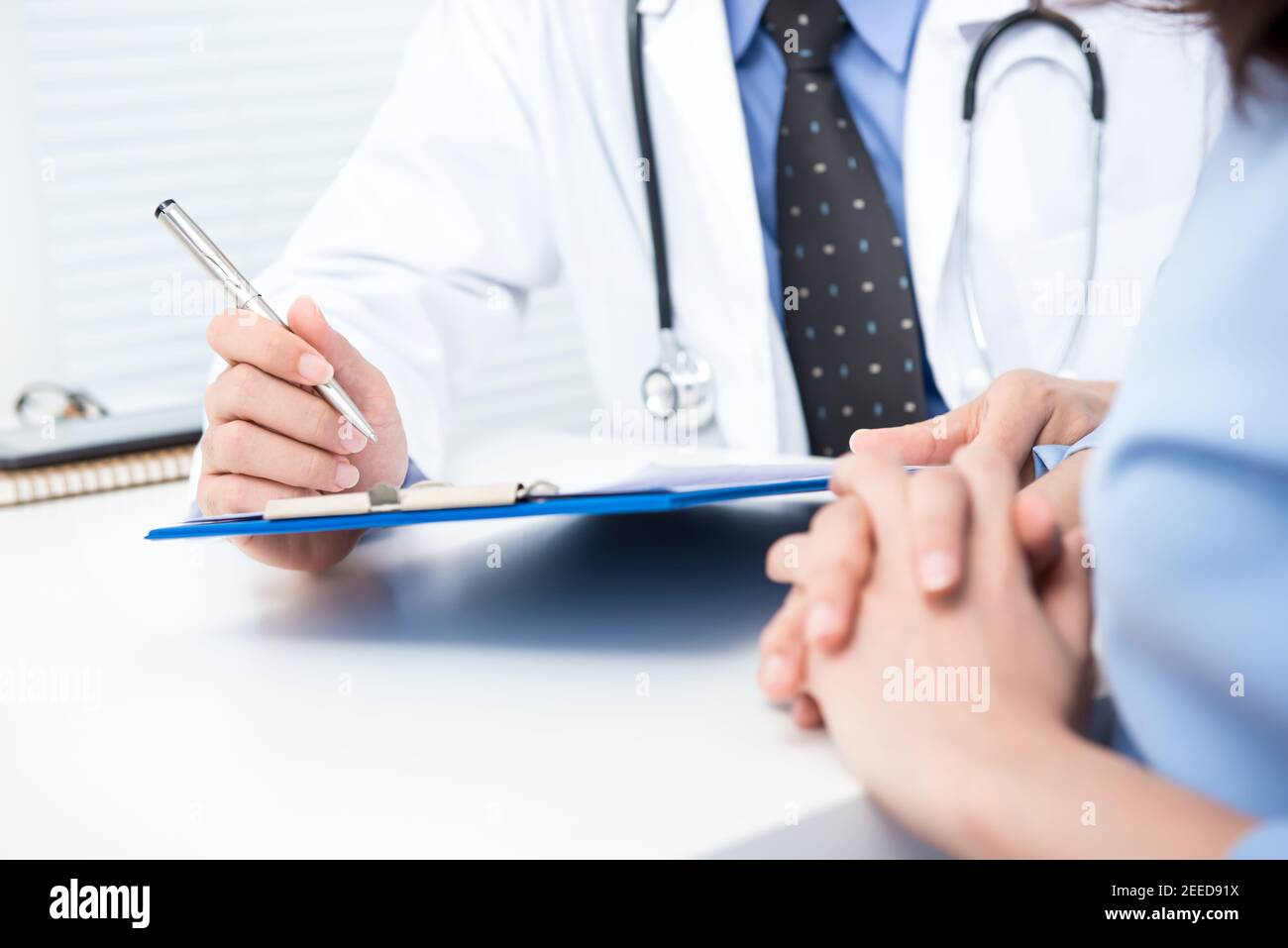 Male doctor noting a female patient medical check up information in ...